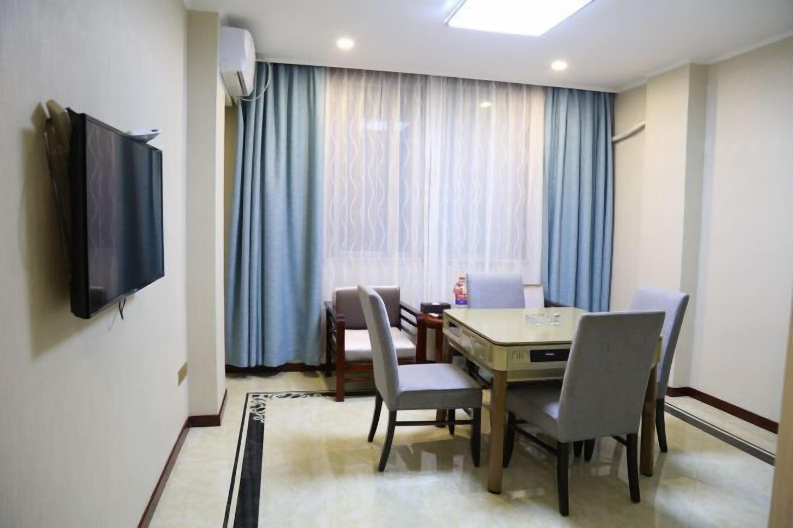 Quarto de hotel com uma mesa de jantar, cadeiras, televisão de tela plana na parede e uma janela grande com cortinas.