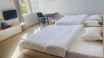 Quarto de hotel com duas camas, uma mesa, uma cadeira, uma televisão e uma janela.