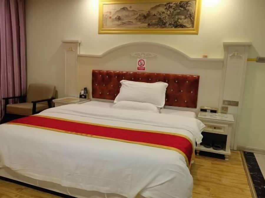 Quarto de hotel com cama, mesa de cabeceira, cadeira, quadro na parede e porta.
