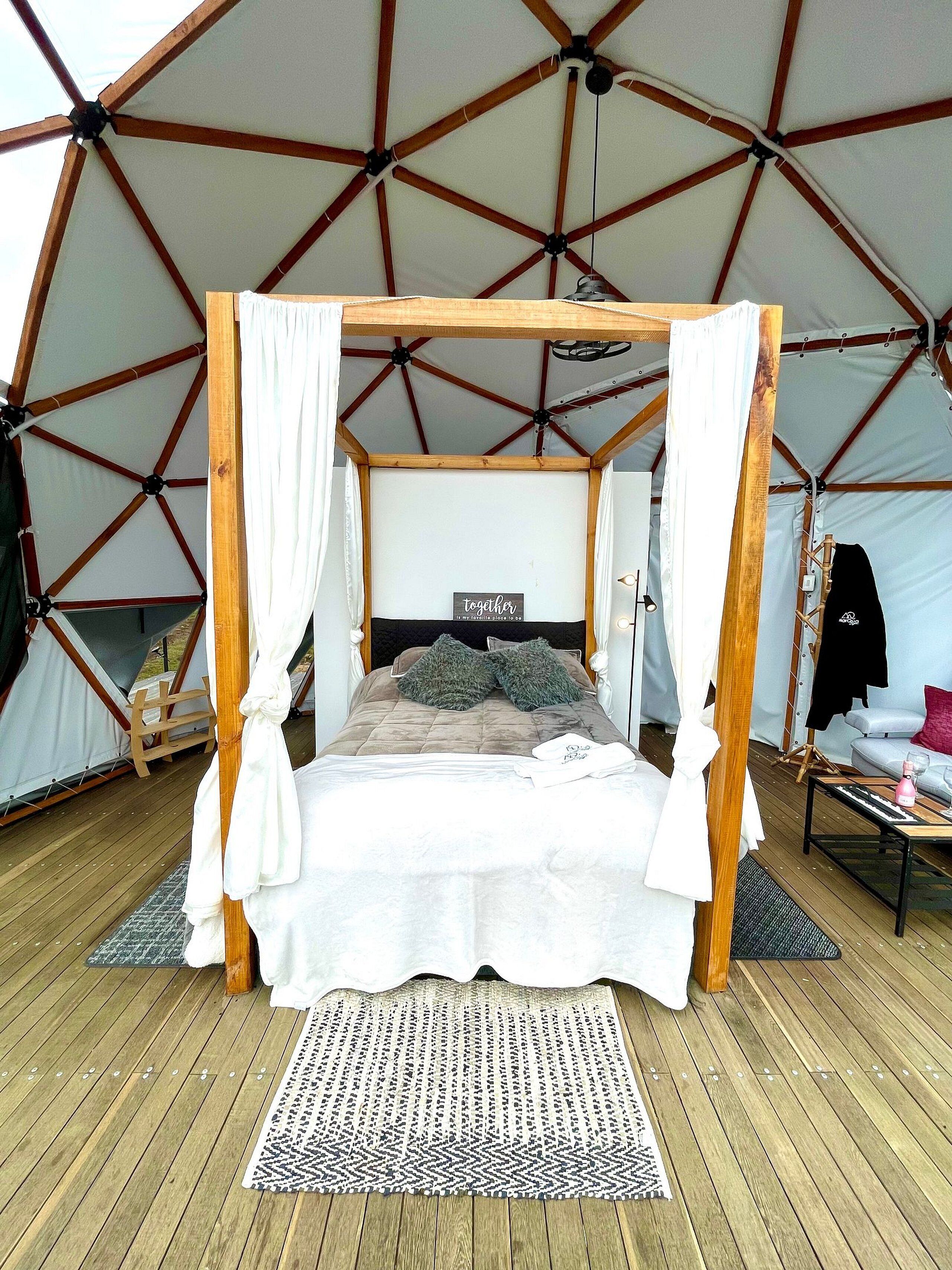 Alojamento em tenda com cama de dossel, soalho de madeira e vista para a área circundante.