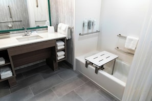 Uma casa de banho moderna com lavatório, espelho, porta-toalhas, chuveiro e uma pequena prateleira com produtos de higiene pessoal.