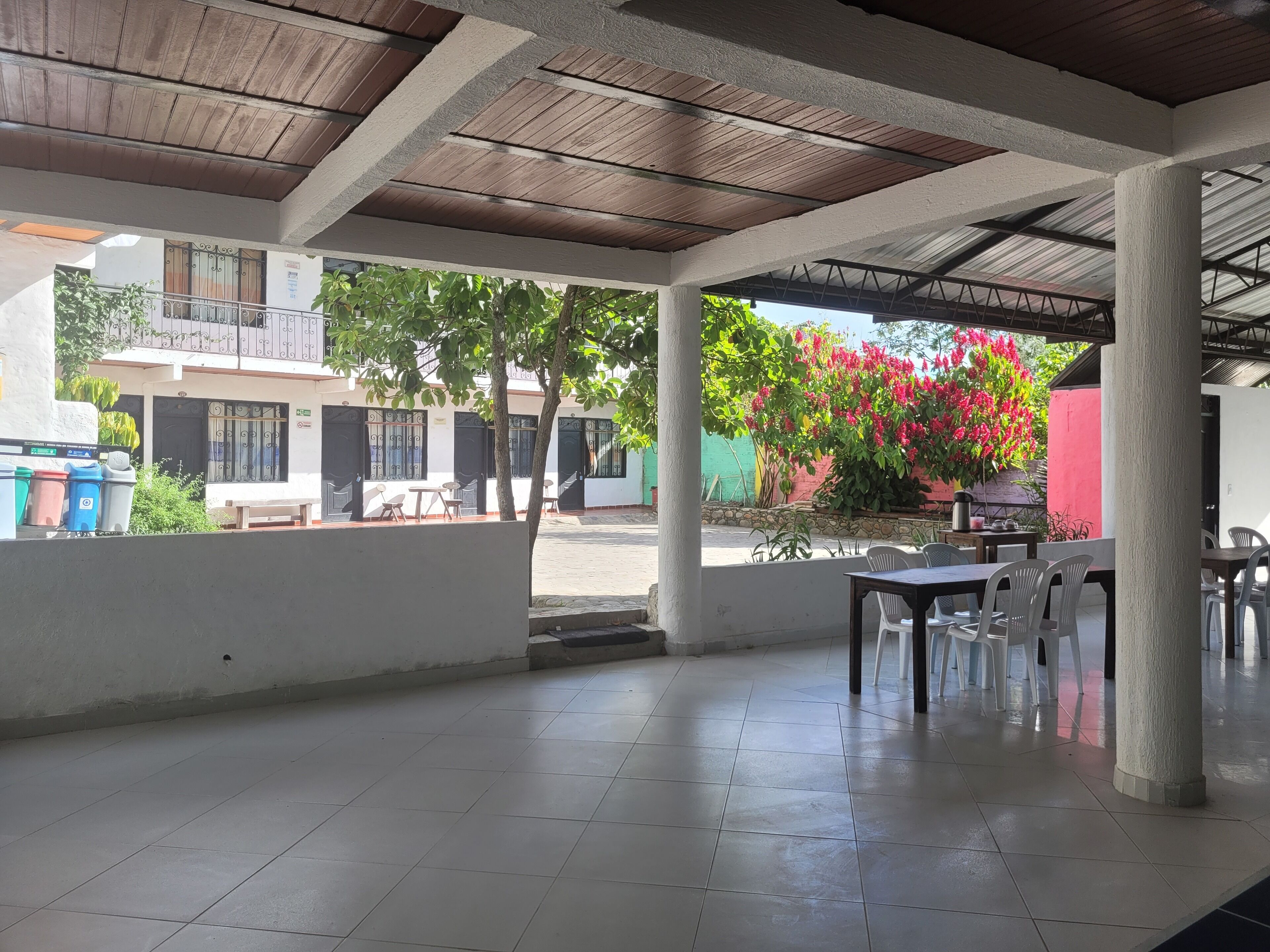 Um pátio coberto ao ar livre com piso de azulejos, assentos externos e vista para um edifício residencial com varanda.