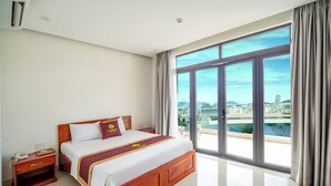 Quarto de hotel com uma cama grande, mesa de cabeceira, telefone e vista para a paisagem urbana através de uma janela ampla.