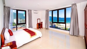 Quarto de hotel com uma cama grande, uma escrivaninha e vista para a praia e oceano.