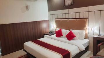 Quarto de hotel com uma cama grande, cabeceira de madeira, tapete listrado em vermelho e branco, ar-condicionado fixado na parede e um quadro emoldurado sobre a cama.