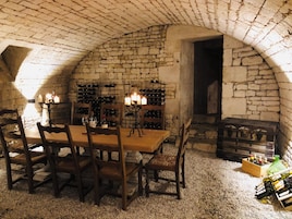 Uma adega rústica com mesa e cadeiras de madeira, cercada por estantes e garrafas de vinho.