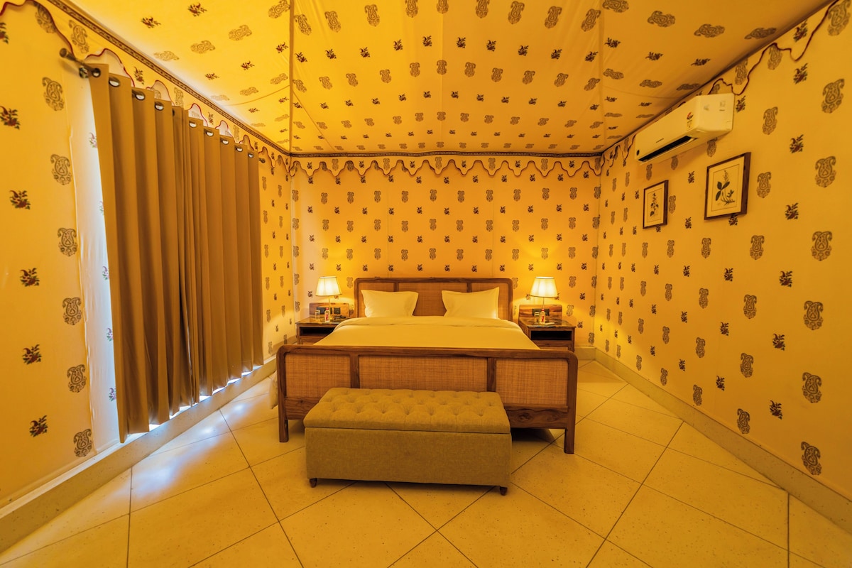 Quarto com uma cama grande, mesa de cabeceira com luminárias, janela com cortinas e papel de parede estampado.
