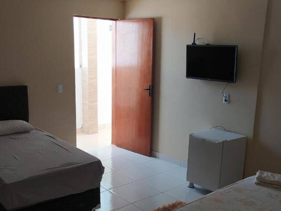 Quarto com cama, televisão na parede e escrivaninha com cadeira.