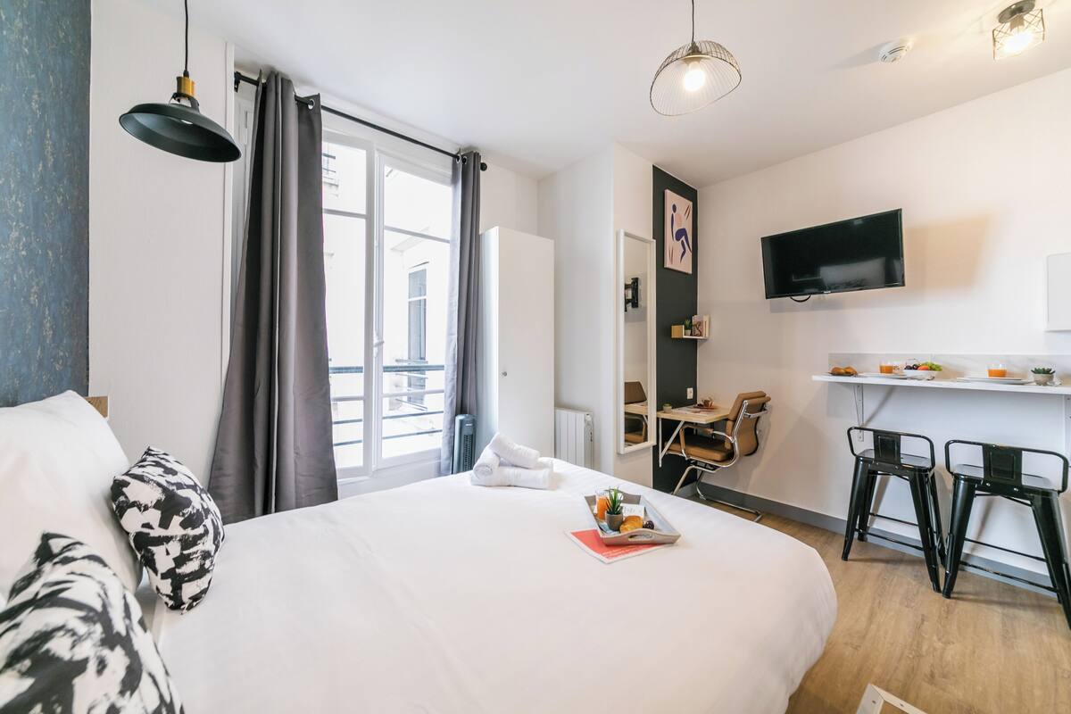 Quarto de hotel com cama, escrivaninha, televisão e bancada de café da manhã.