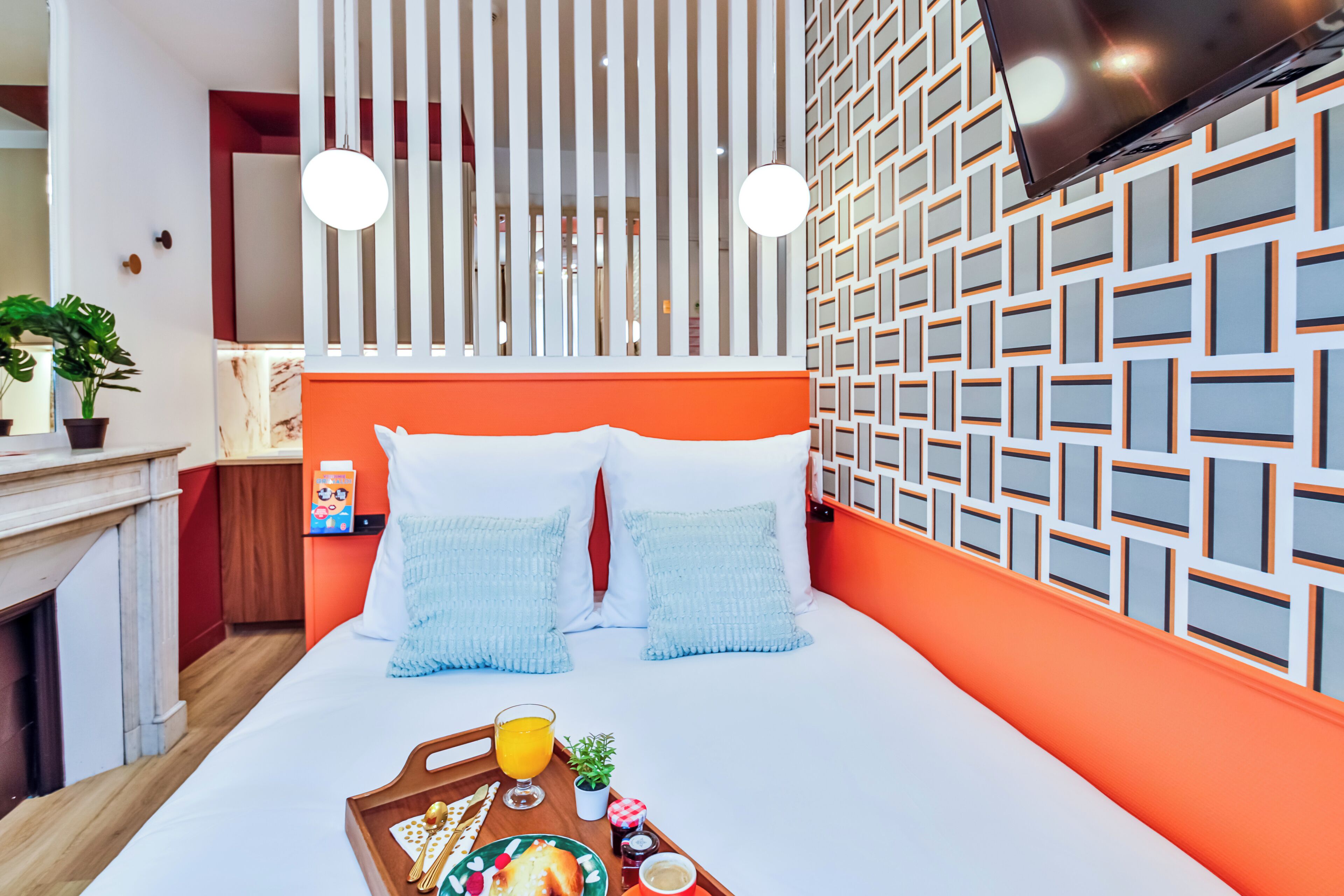 Quarto de hotel moderno com cama, cabeceira laranja e bandeja de café da manhã na cama.