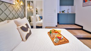 Quarto de hotel com cama, bandeja com itens de café da manhã, área de cozinha e porta que dá para outro cômodo.