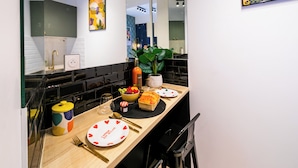 Cozinha moderna com bancada de madeira, pia e espelho. Há diversos utensílios de cozinha na bancada, incluindo uma tigela com frutas, uma garrafa de molho e uma planta.