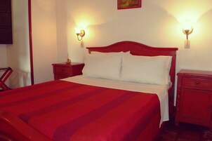 Uma cama bem arrumada com colcha listrada em vermelho e branco, duas mesas de cabeceira com abajures e um quadro pendurado na parede acima da cama.