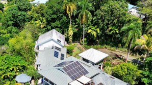 Vista aérea de um resort com piscina, painéis solares e vegetação exuberante.
