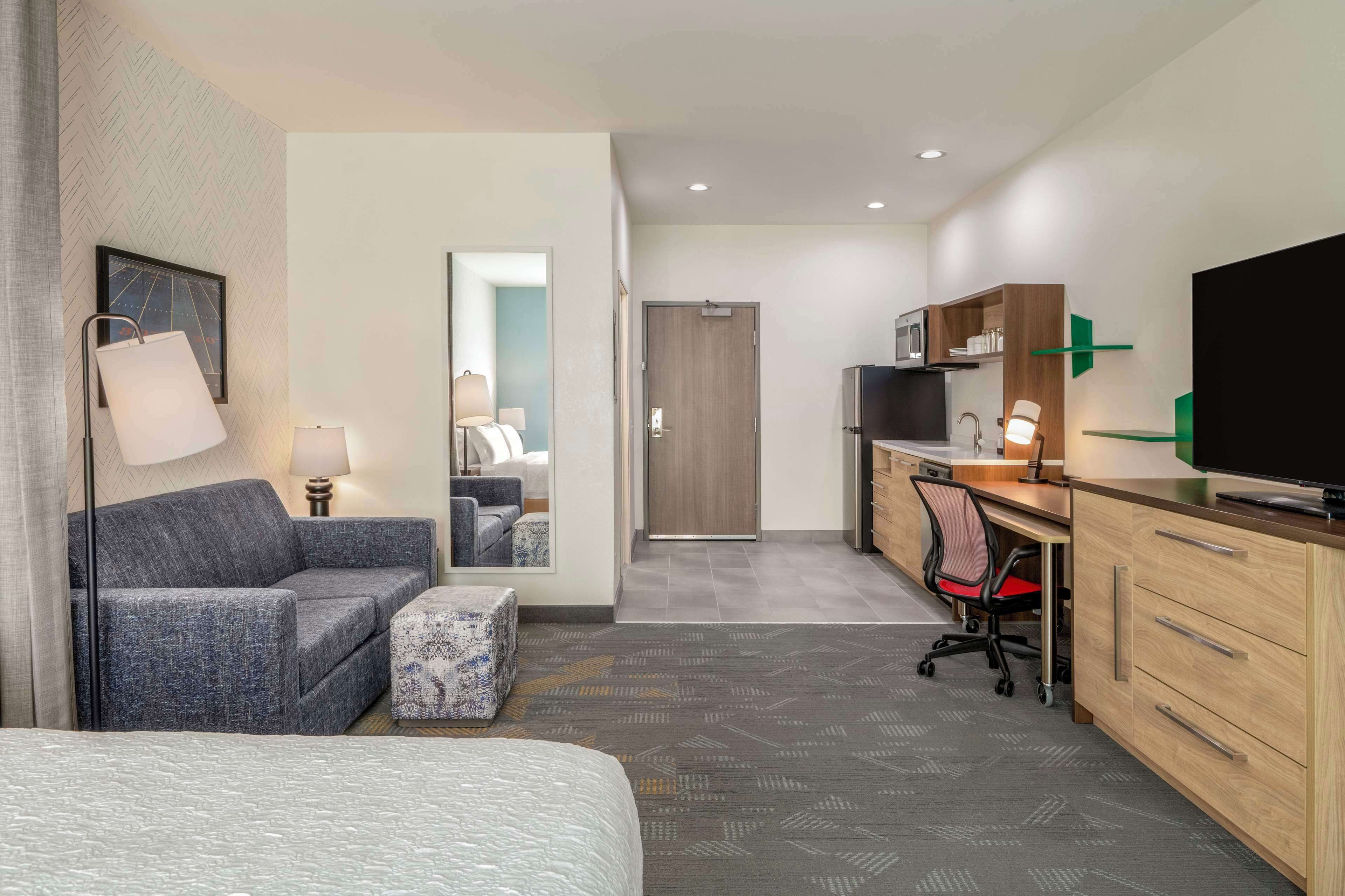 Quarto de hotel com cama, sofá, escrivaninha com computador, televisão e micro-ondas.
