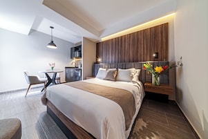 Quarto de hotel moderno com uma cama grande, uma escrivaninha e uma cozinha compacta.