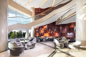 Um hall espaçoso com teto alto, assentos modernos e uma parede diferenciada com luminárias pendentes.