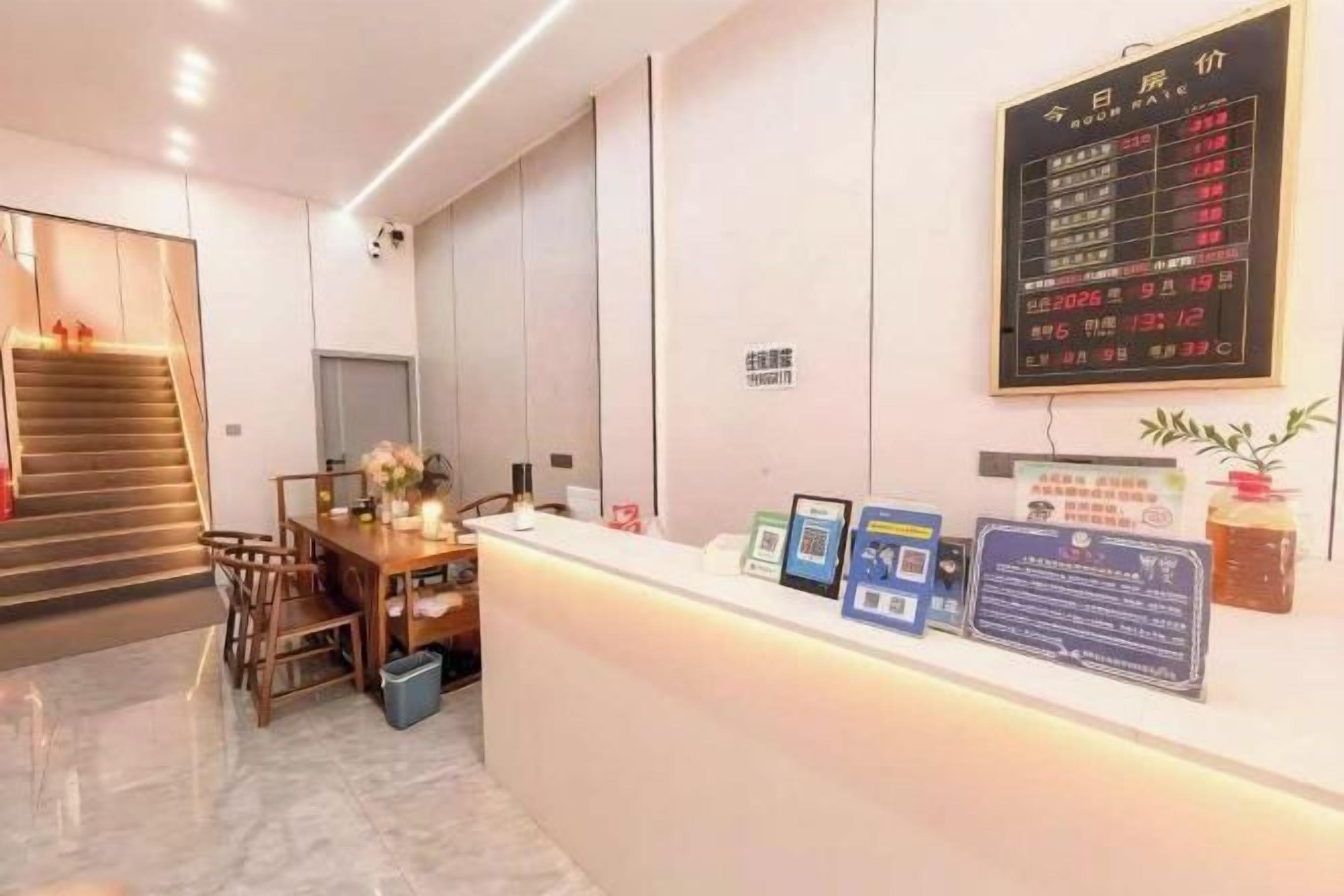 Uma área de recepção de hotel com balcão, painel de exibição digital, escada e área de refeições.