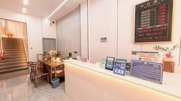 Uma área de recepção de hotel com balcão, painel de exibição digital, escada e área de refeições.