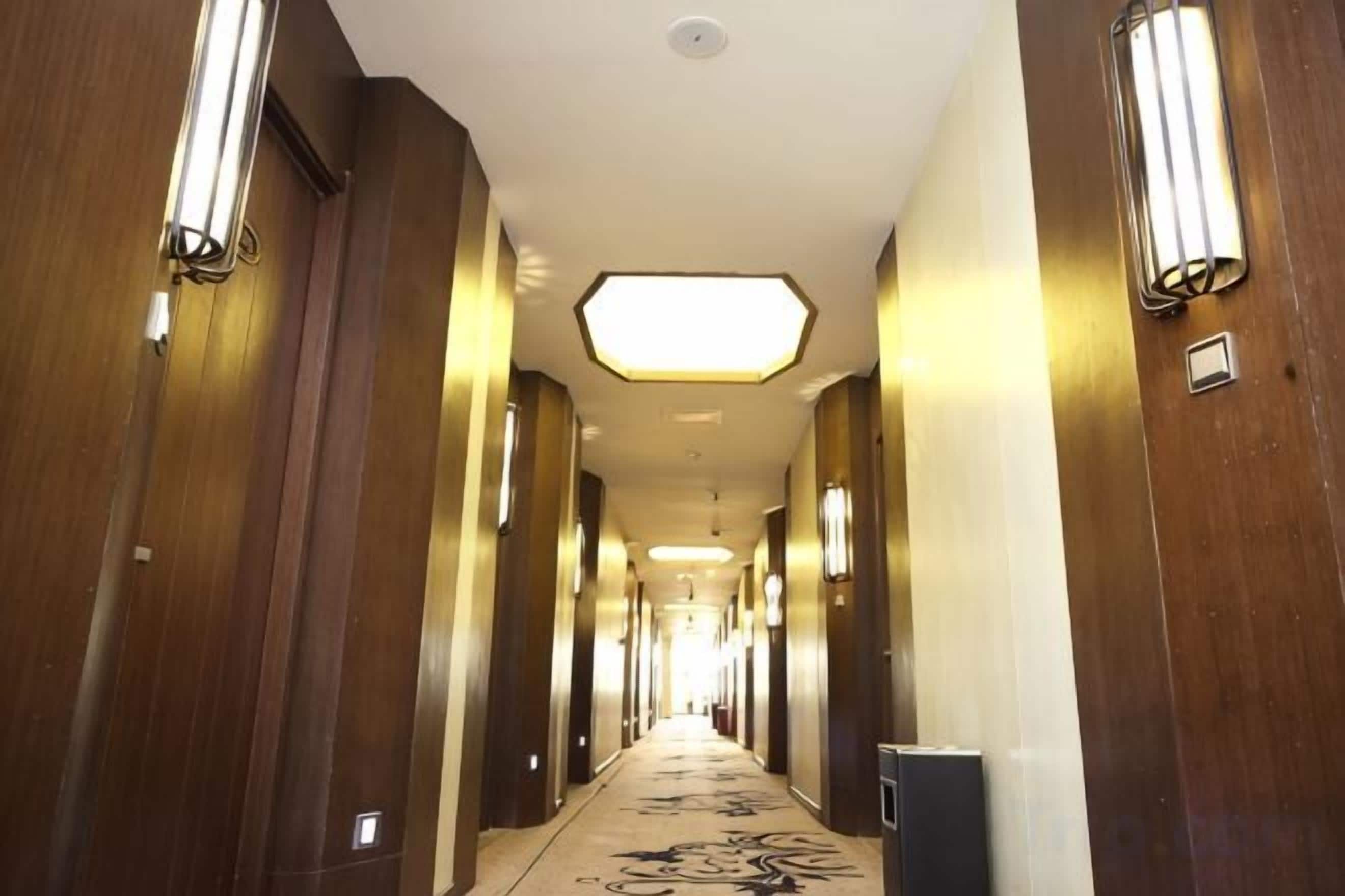 Um corredor comprido e estreito, com paredes de madeira e carpete estampado, que leva a uma luminária hexagonal clara.