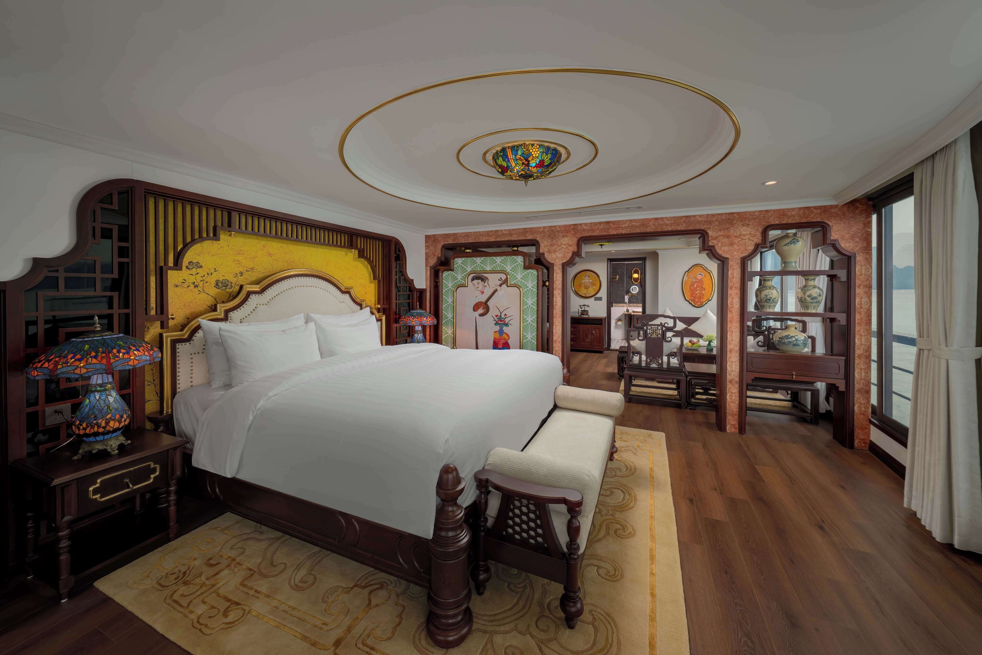 Quarto tradicional com uma cama grande, um banquinho, uma mesa de cabeceira e um abajur decorativo.