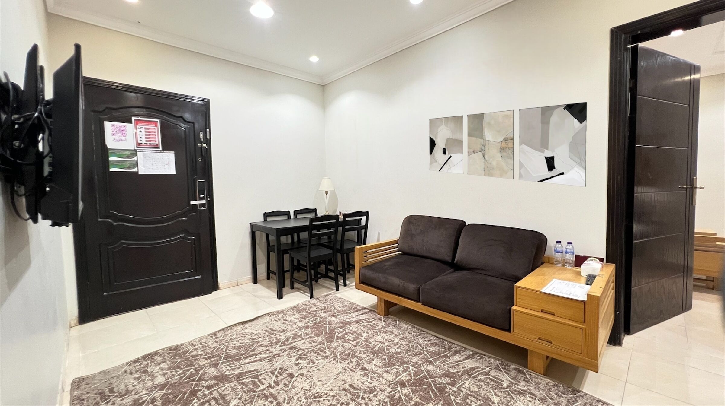 Espaço compacto com sofá, mesa de jantar com cadeiras, tapete pequeno e porta com aviso.