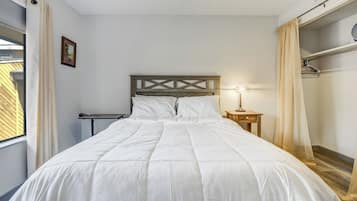Uma cama bem arrumada com cabeceira de madeira, mesa de cabeceira com abajur e janela com cortinas.