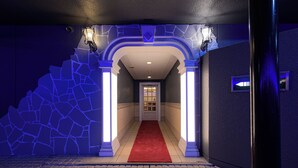Um corredor com carpete vermelho, parede azul com padrão de mosaico e duas luminárias fixadas na parede.