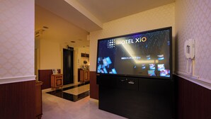 Um saguão de hotel com uma tela grande exibindo 'HOTEL XIO' e um balcão de recepção.