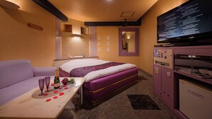 Quarto de hotel com cama, televisão, sofá e minibar.