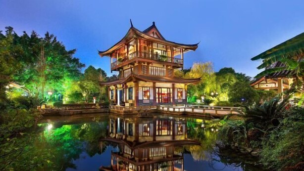 Um edifício tradicional de vários andares refletido na água, rodeado por vegetação exuberante.