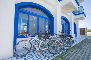 Um edifício moderno com arquitetura azul e branca, com grandes janelas e área de entrada coberta por azulejos, onde bicicletas estão estacionadas.