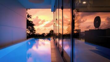 Uma área moderna de piscina interna com paredes de vidro, vista clara do pôr do sol e uma antena parabólica grande.