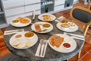 Uma mesa de jantar redonda com diversos pratos indianos, utensílios e uma cadeira.