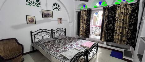 Quarto com cama, cadeira, ventoinha no teto e janela com cortinas.