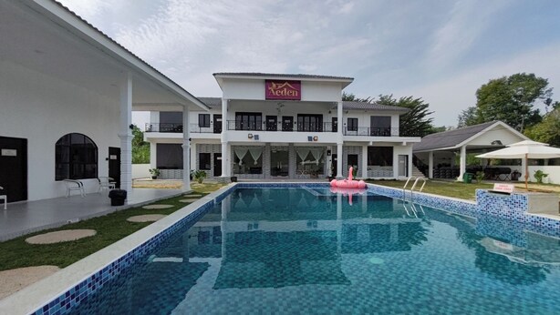 Um hotel de dois andares com piscina, um alpendre coberto e uma placa com a inscrição 'Aeden'.