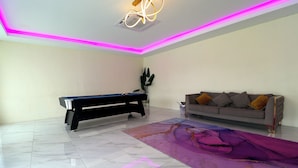 Uma sala de estar moderna com mesa de bilhar, um sofá com almofadas e um tapete grande e abstrato.