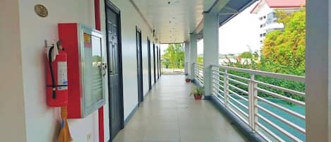 Corredor com portas, um extintor e guarda-corpo com vista para o verde.