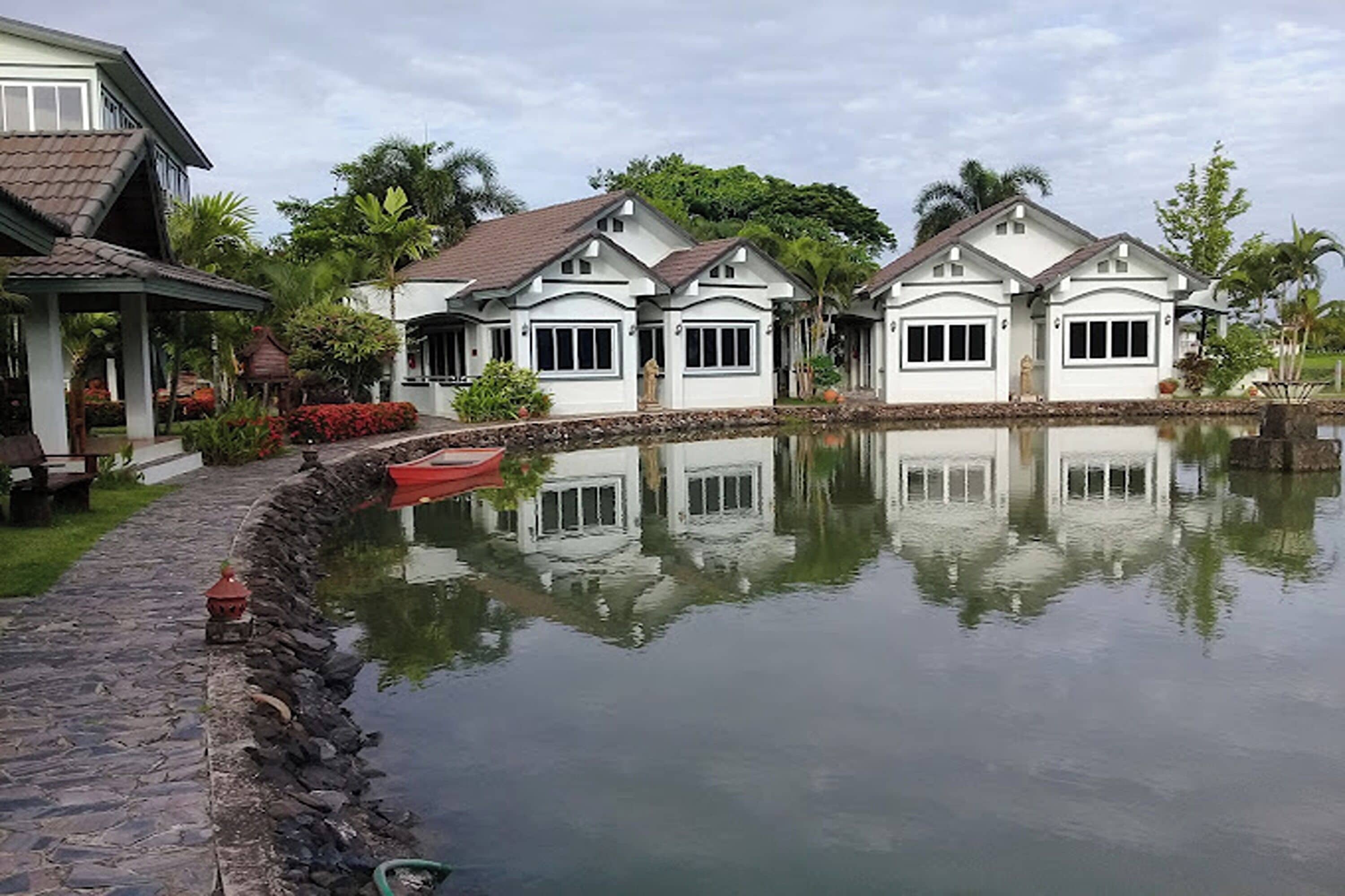 Um imóvel tranquilo à beira-mar com três casas brancas, um caminho de pedra e um lago calmo que reflete as construções.
