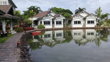 Um imóvel tranquilo à beira-mar com três casas brancas, um caminho de pedra e um lago calmo que reflete as construções.