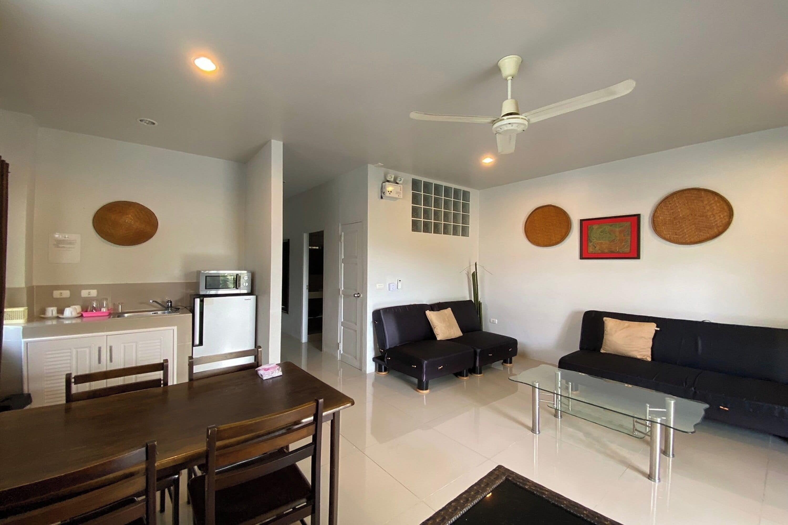 Uma sala de estar moderna com um sofá preto, uma mesa de centro de vidro e um espaço de jantar com mesa e cadeiras de madeira.
