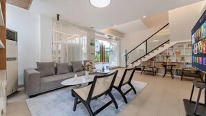 Uma sala de estar moderna com sofá, mesa de centro e cadeiras, uma escada e uma estante de livros.