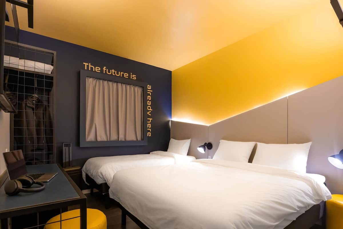 Quarto de hotel moderno com uma cama grande, uma escrivaninha com um laptop, uma cadeira e um guarda-roupa.
