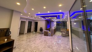 Um saguão de hotel moderno com piso de mármore, iluminação embutida e uma área de estar com uma máquina de café.