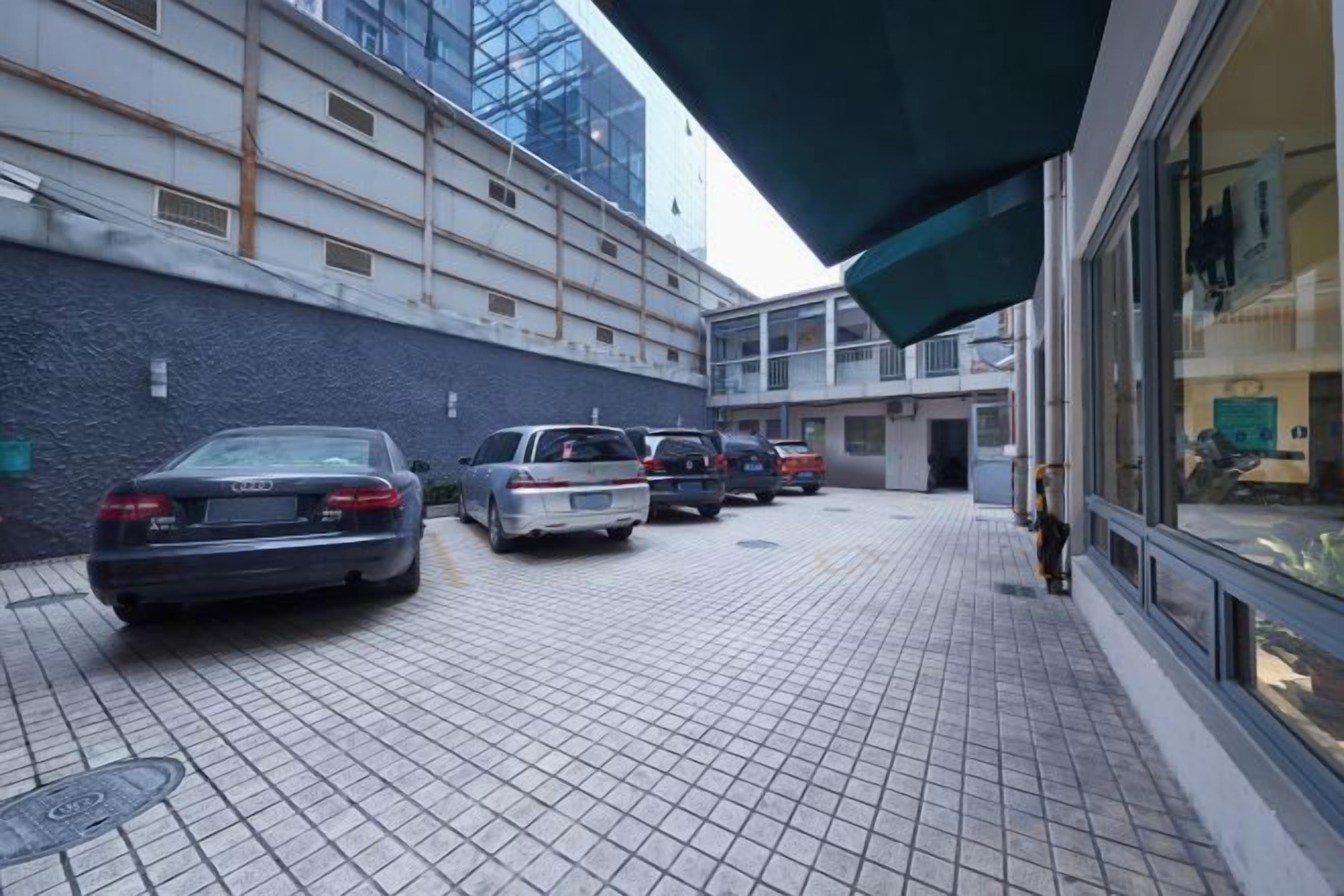 Uma área de estacionamento com vários carros estacionados em frente a um edifício com chão de azulejos e fachada de vidro.