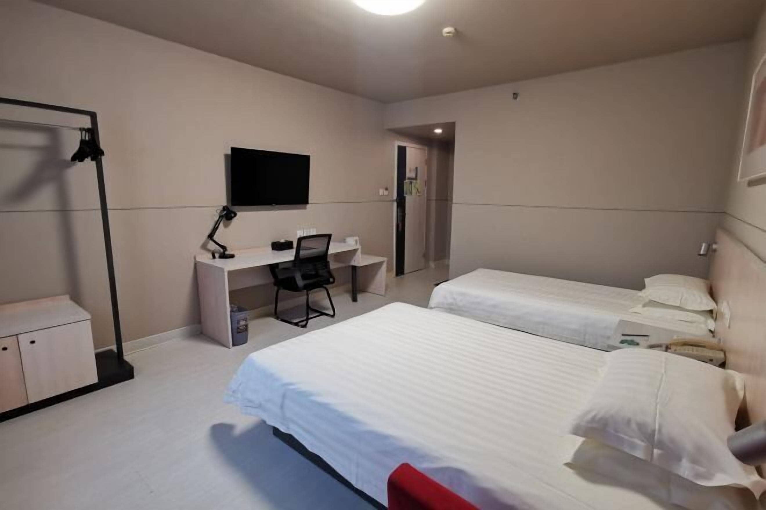 Quarto de hotel com duas camas, uma escrivaninha com cadeira, uma televisão e um guarda-roupa.
