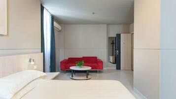 Quarto de hotel moderno com cama, sofá vermelho, mesa redonda pequena e planta.
