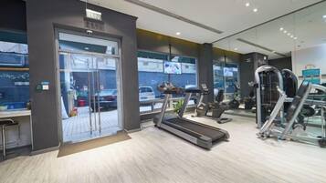 Academia com equipamentos de ginástica, esteira e porta que dá para o exterior.