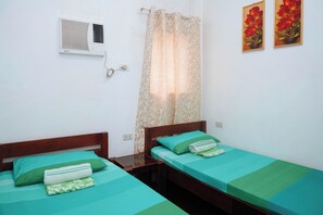 Quarto com duas camas de solteiro, cada uma com roupa de cama e almofadas verdes, cabeceira de madeira, mesa de cabeceira pequena e ar-condicionado fixado na parede.