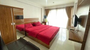 Quarto de hotel com uma cama grande, guarda-roupa, secretária, cadeira, televisão e janela com cortinas.